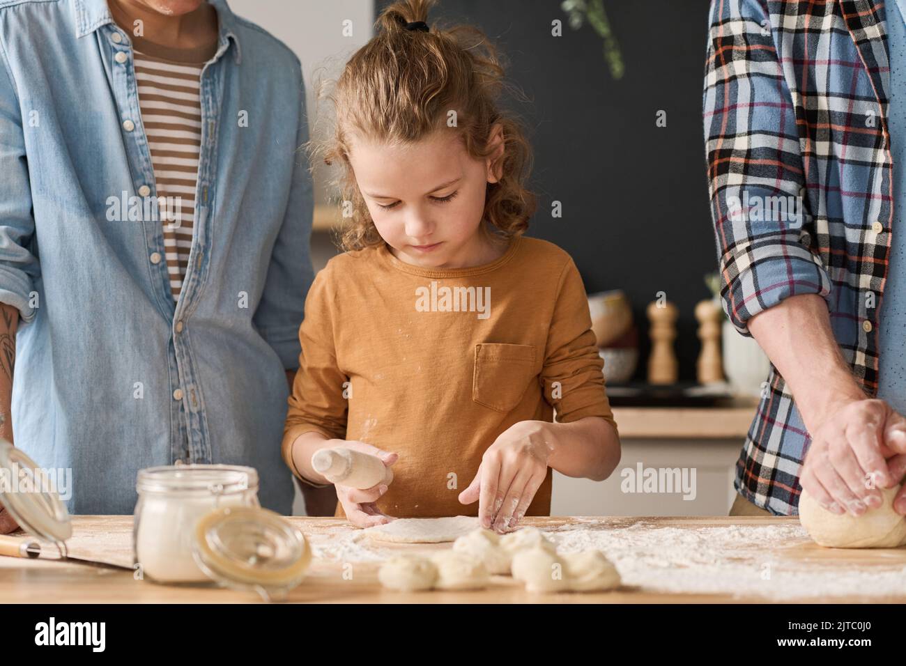 Little boy learning to bake pie from dough together with his parents at ...