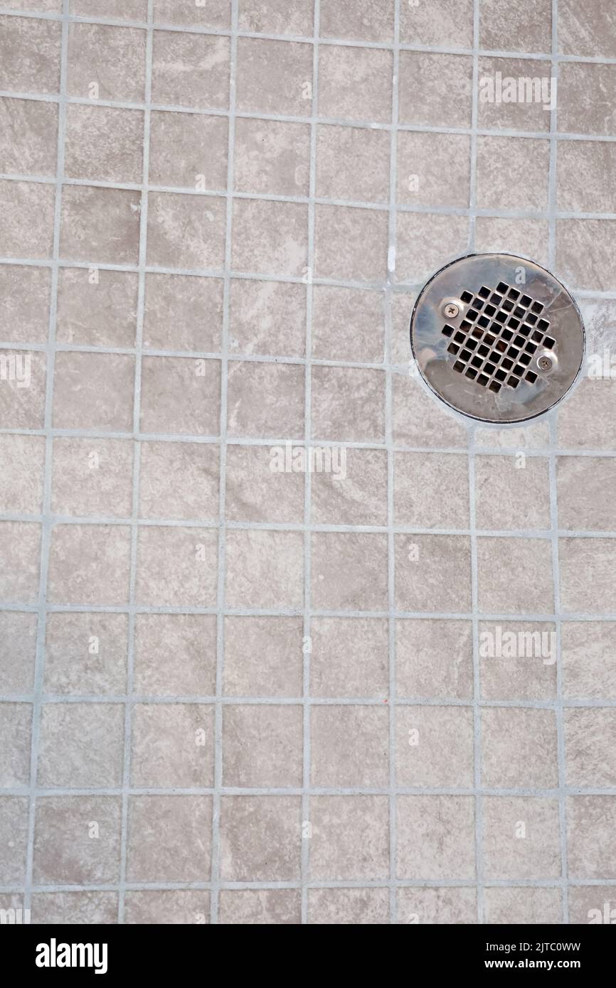 A neutral light beige square tile shower floor with a silver metal ...