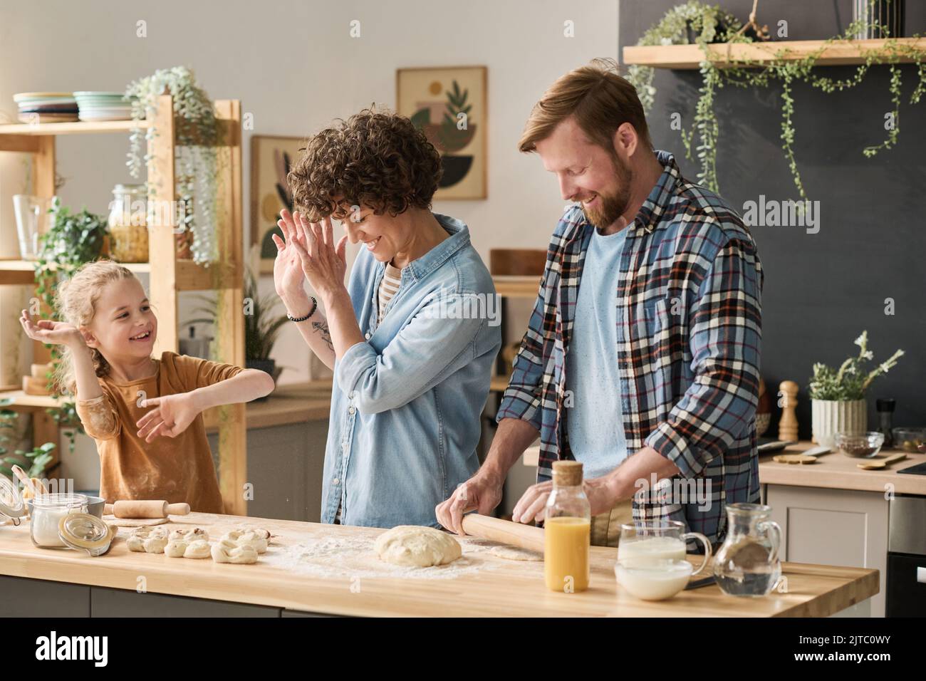 Mother and son having fun in kitchen while dad rolling dough for buns ...