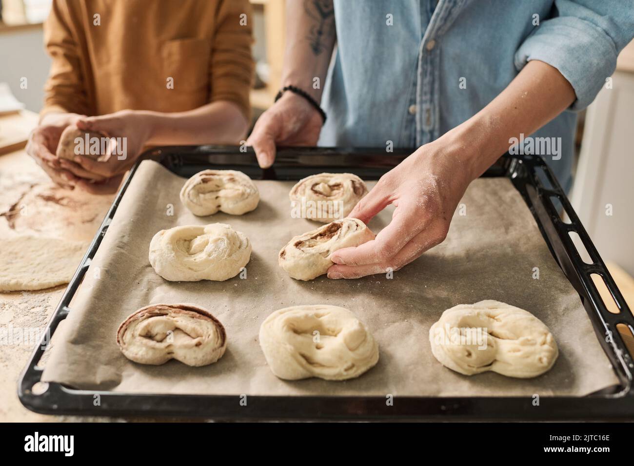 Close-up of mother putting homemade buns on tray for baking with her ...