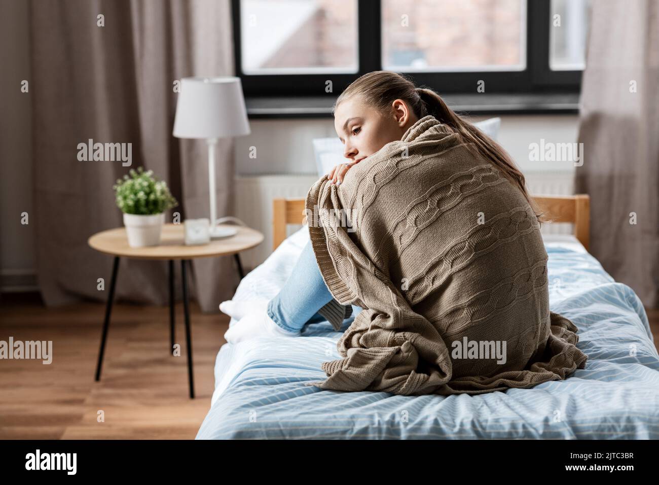 sad girl in blanket sitting on bed at home Stock Photo - Alamy