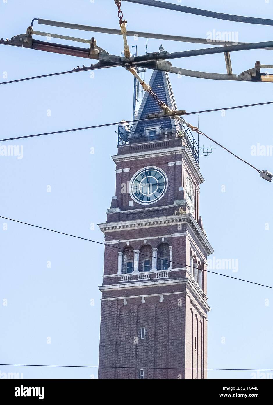 Tall brick tower with clock behind overhead tram and power lines ...