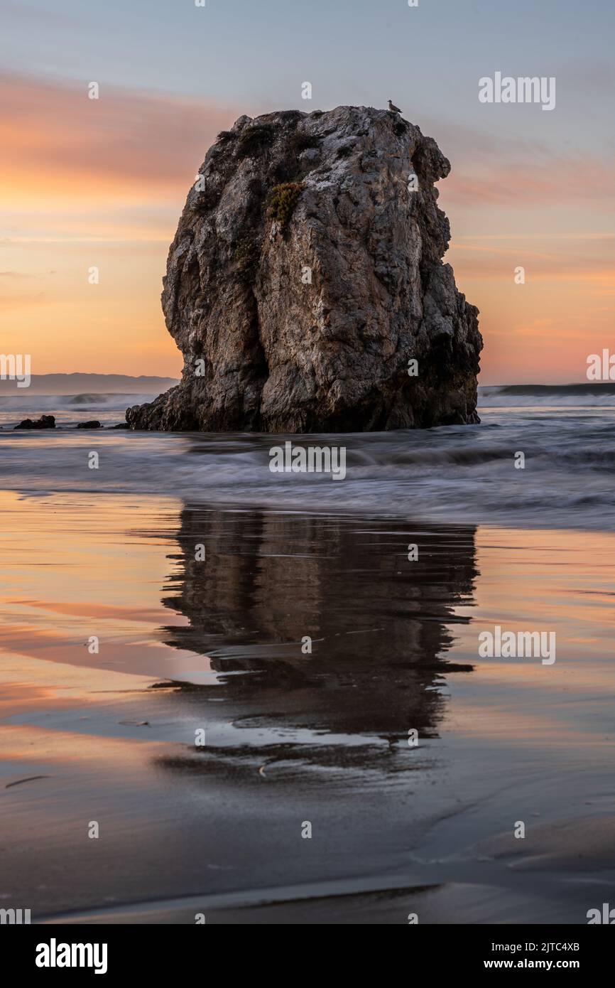 A vertical scenic view of the golden sunset over bid rock in seawater ...