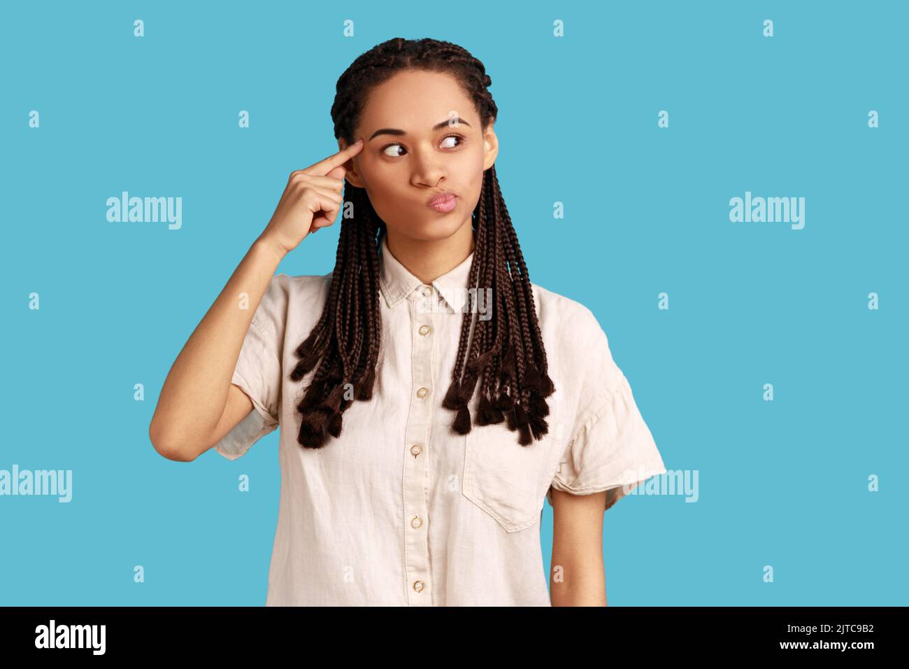 Positive woman with black dreadlocks holding finger near head temple ...