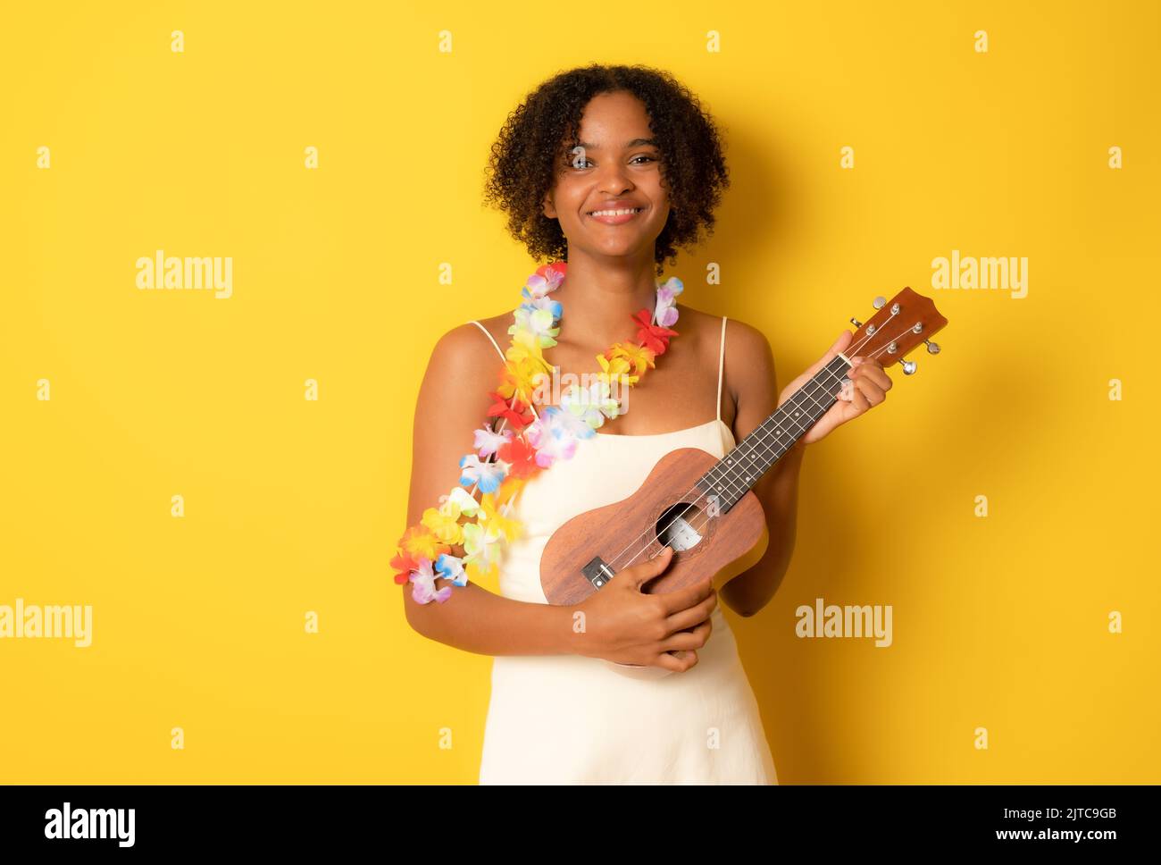 Cute african woman playing ukulele wearing flower lei necklace standing ...