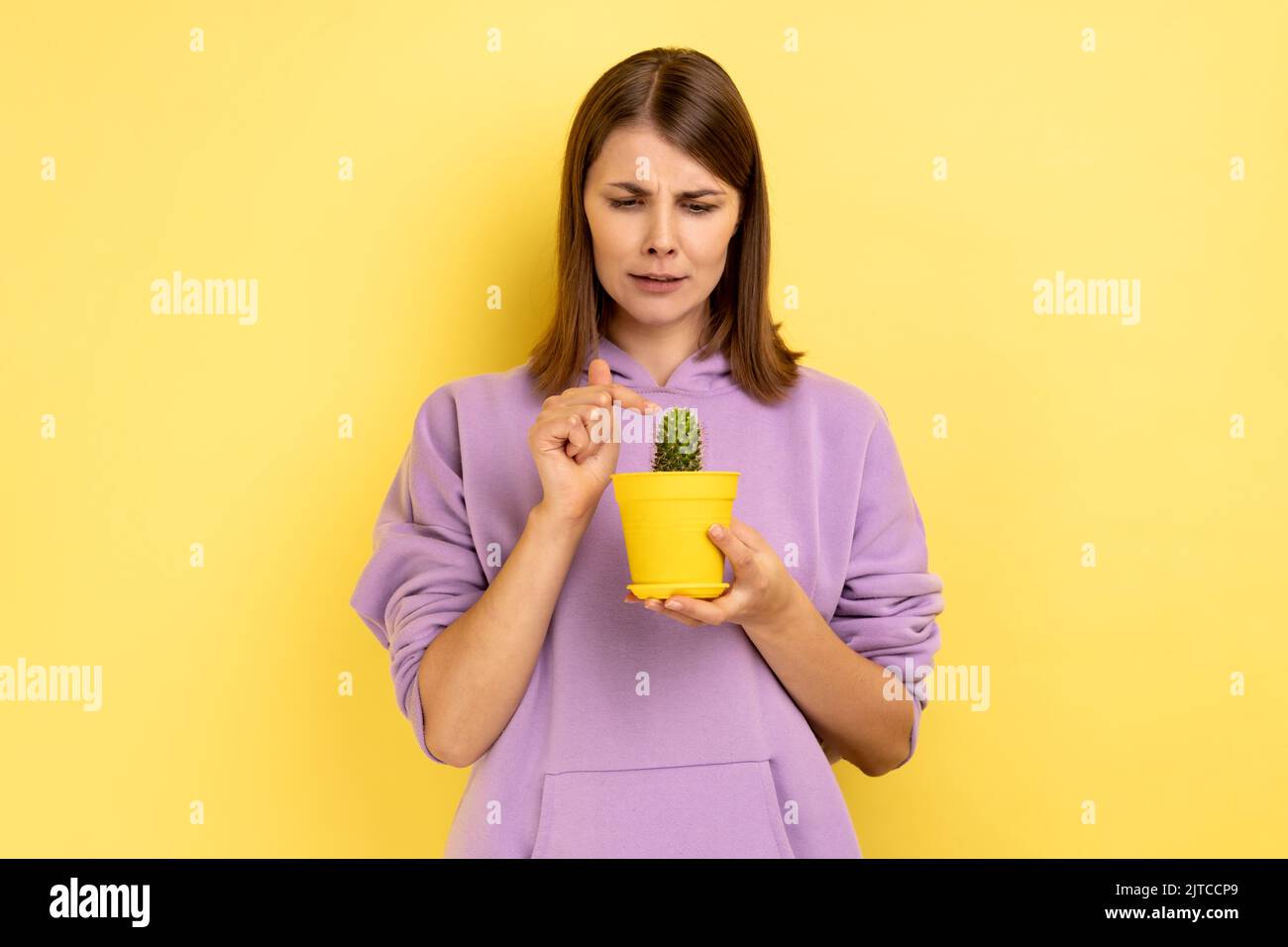 Portrait of young adult woman holding prickly cactus, touching it with ...