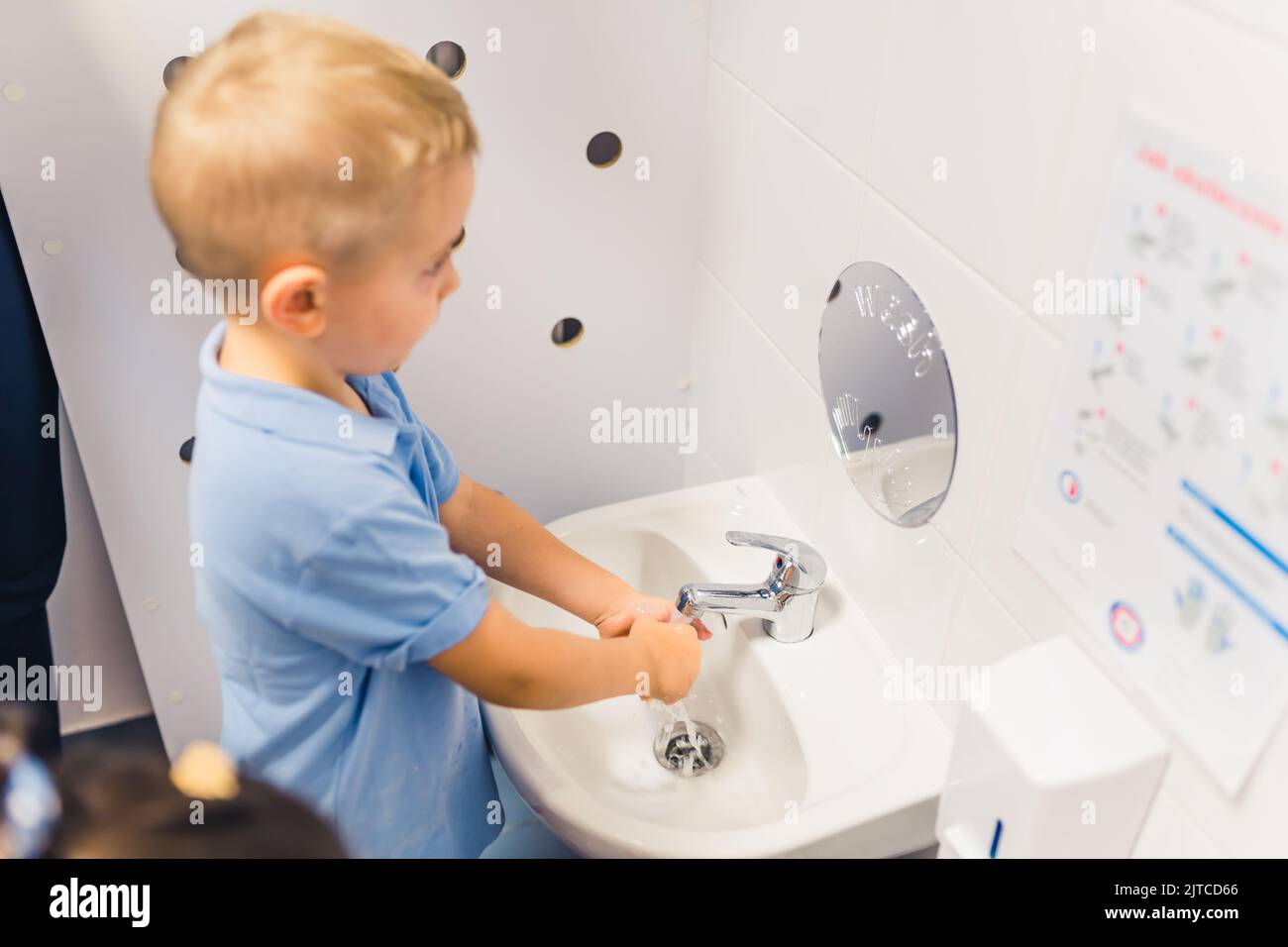 Toddler boy washing his hands with soap after playtime at the nursery ...