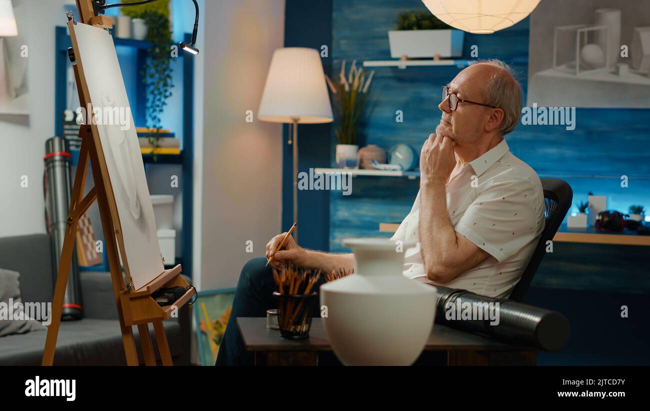 Old artist looking at vase inspiration to create artwork sketch, using ...