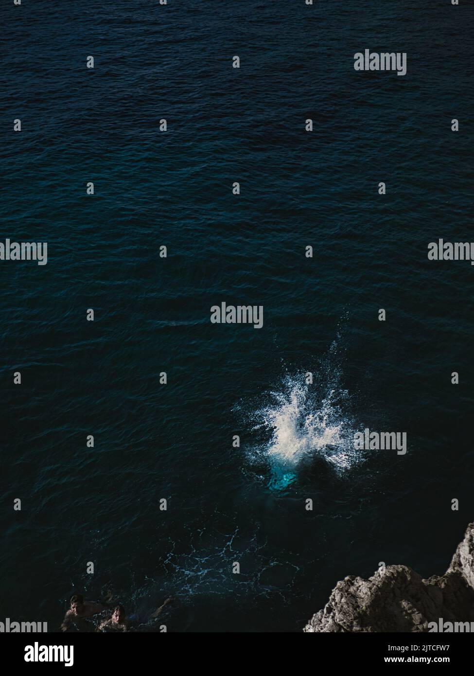 A view of people in a sea and water splashes after male jumping from a ...