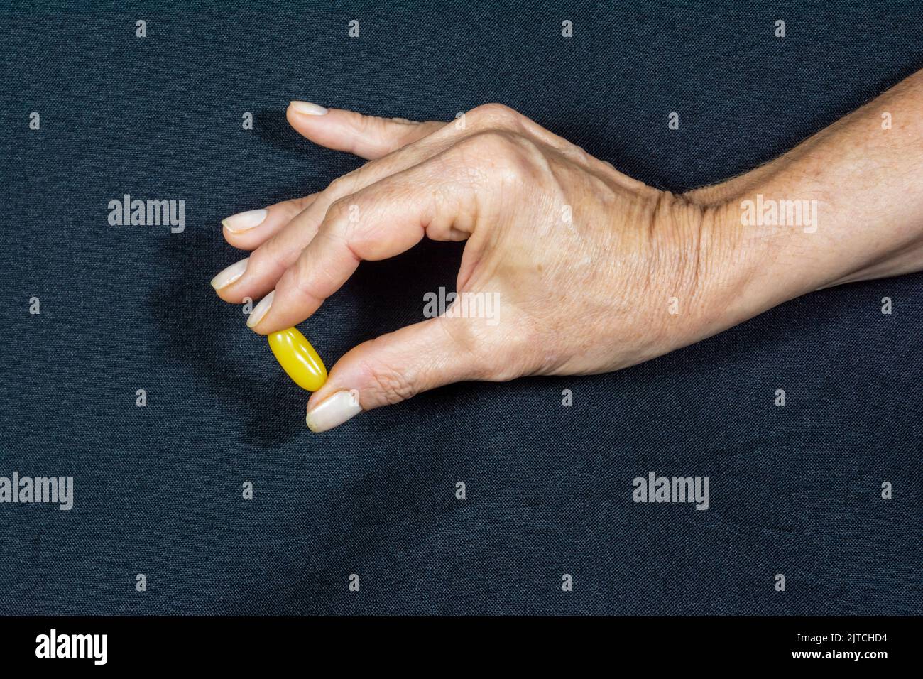 A yellow pill held by the fingers of one hand against a black ...