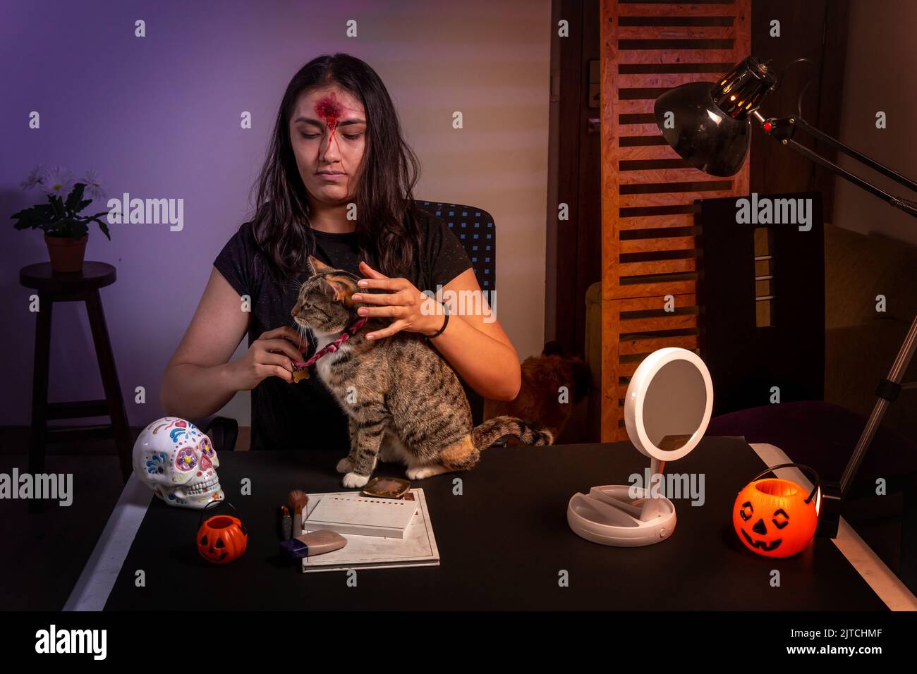 Teenage girl playing with her cat and putting on halloween makeup with ...