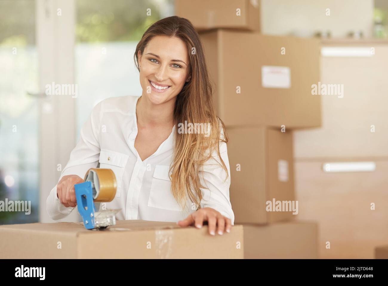 Heres to a new start. Portrait of a smiling young woman packing boxes ...