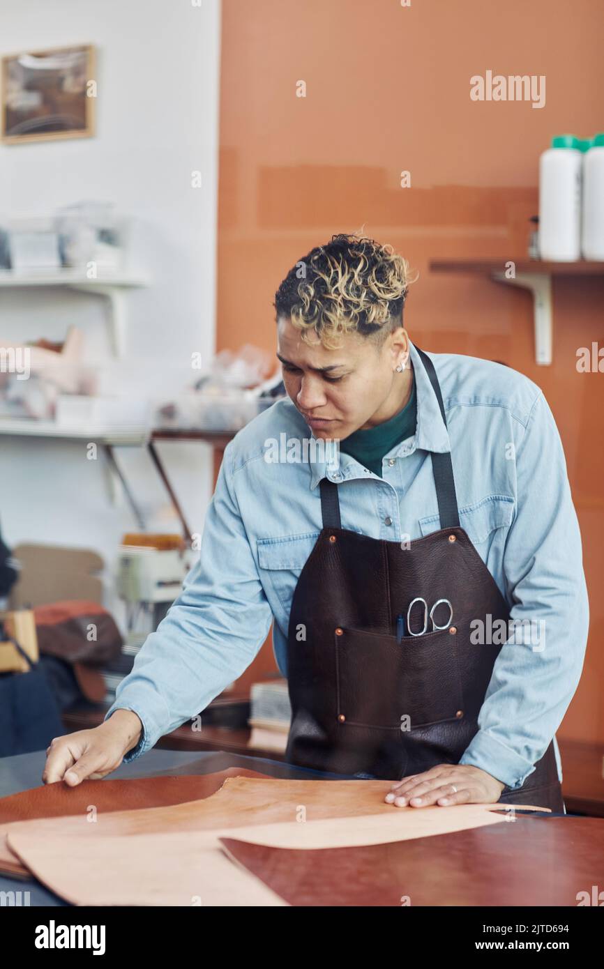 Vertical portrait of young craftsman working with leather in tannery ...
