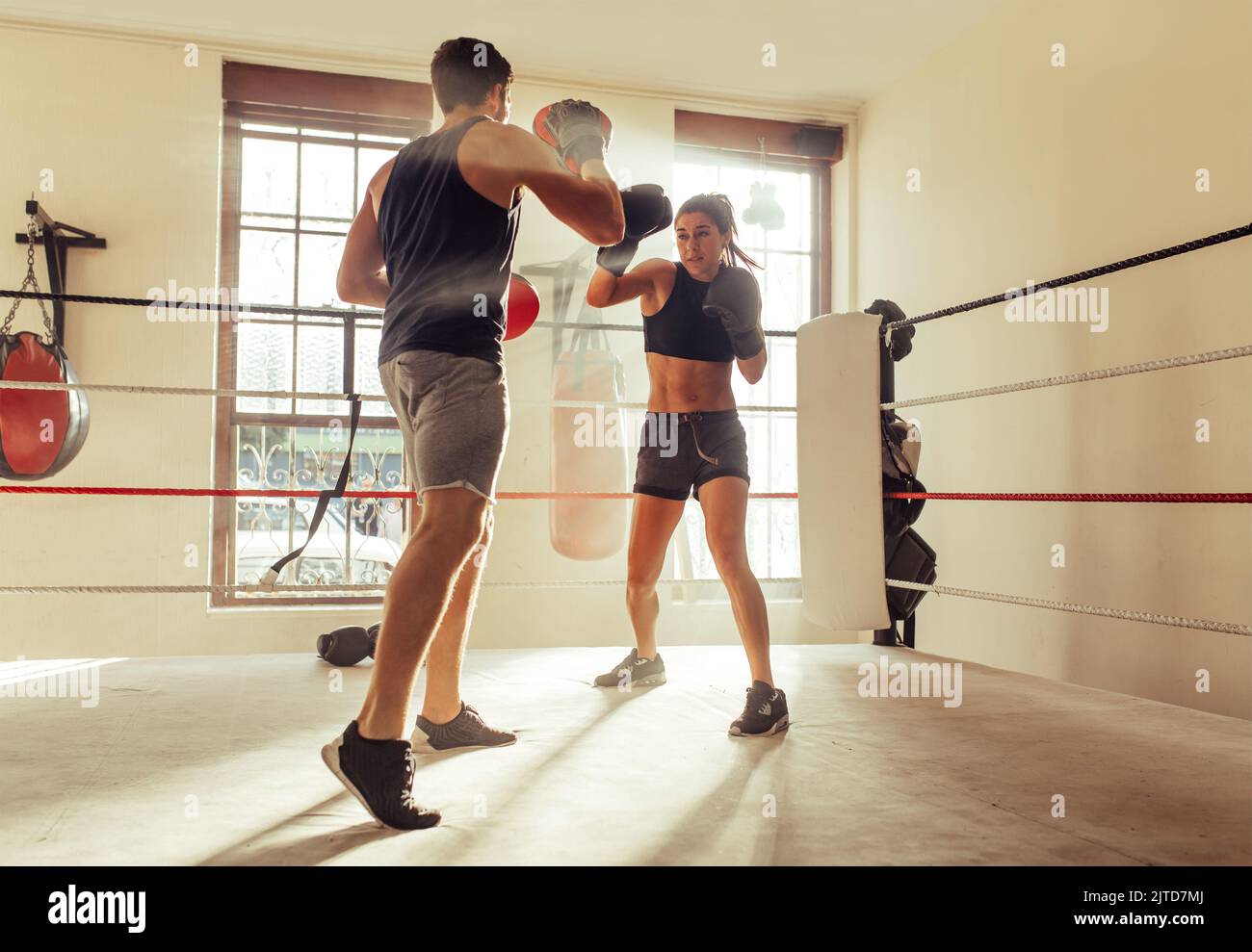 Male trainer helping young female boxer with striking techniques in a ...