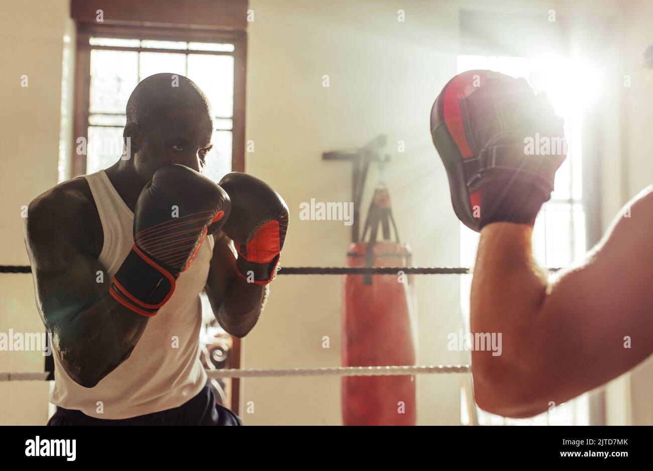 Focused boxer facing a punching mitt held by his personal trainer ...