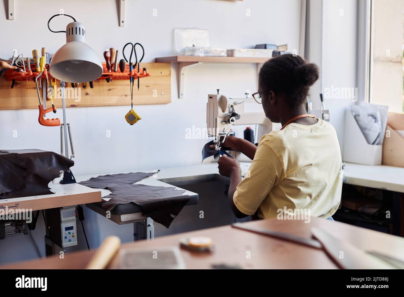Back view of young woman using sewing machine and creating handmade ...
