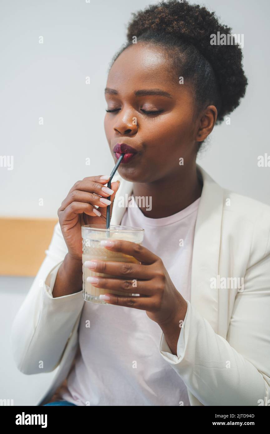 Close-up view of an African woman sitting in cafe and drinking frappe ...