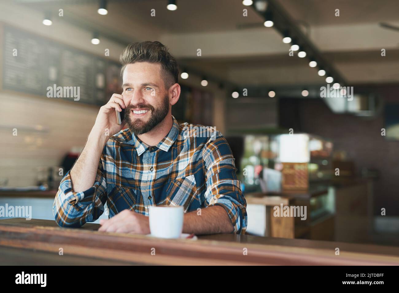 Join me for coffee. a young man talking on his cellphone while sitting ...