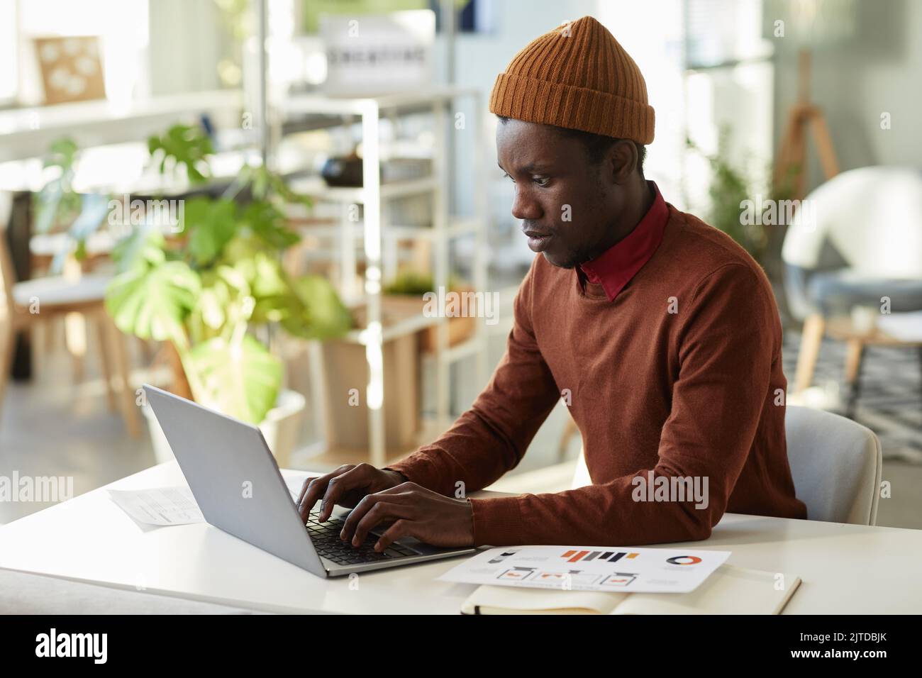 Side view portrait of young black man working with laptop at office ...