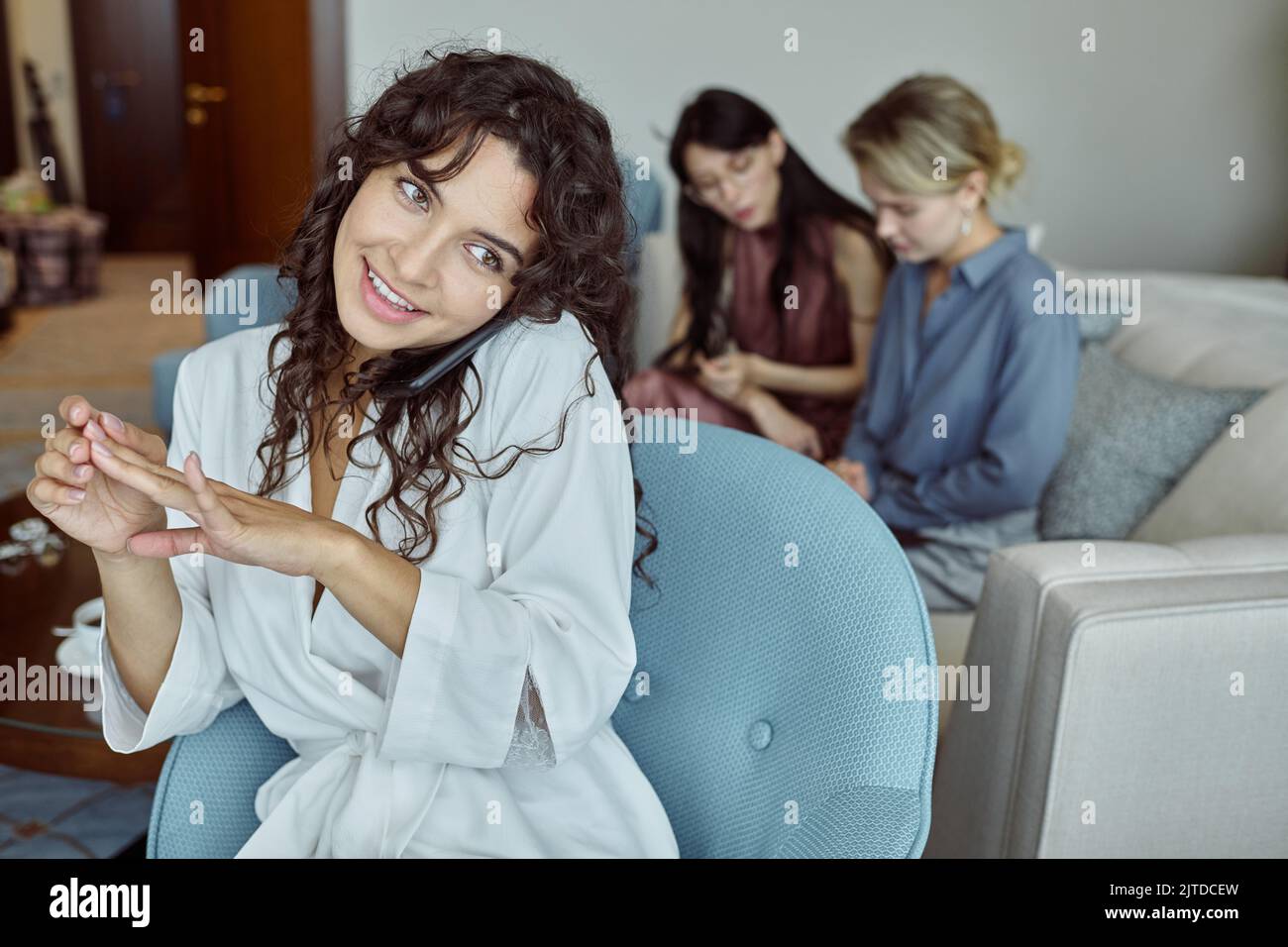 Young smiling brunette woman in white bathrobe with mobile phone ...