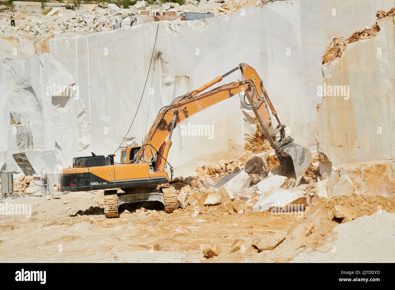 Industrial machine grabbing one of several huge white marble rocks ...