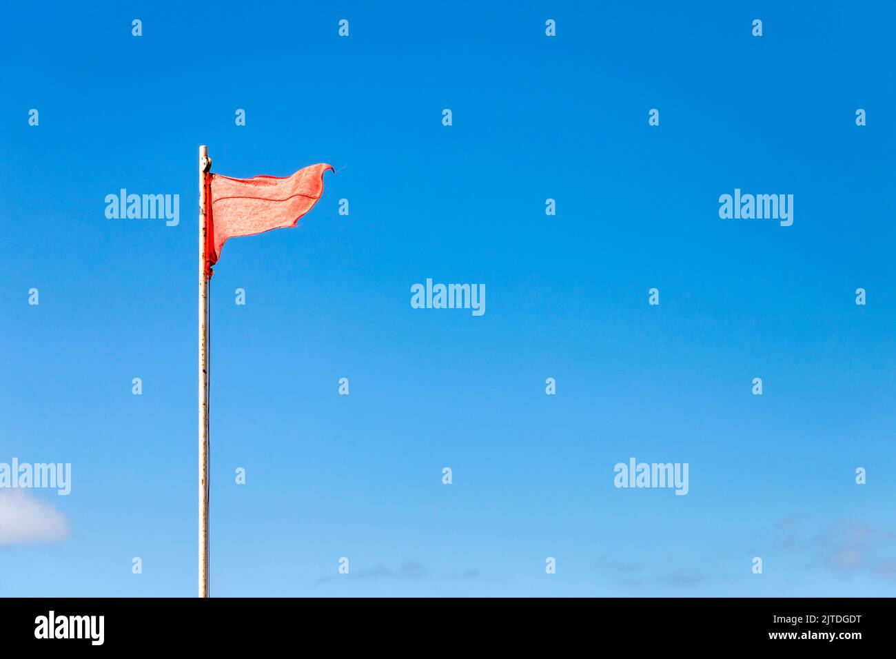 Red warning flag waving on wind under blue sky Stock Photo - Alamy