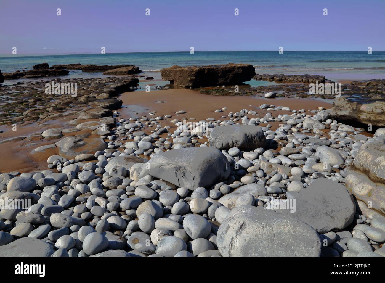 A day on the beach as the tide goes out leaving large rocks, sand and ...