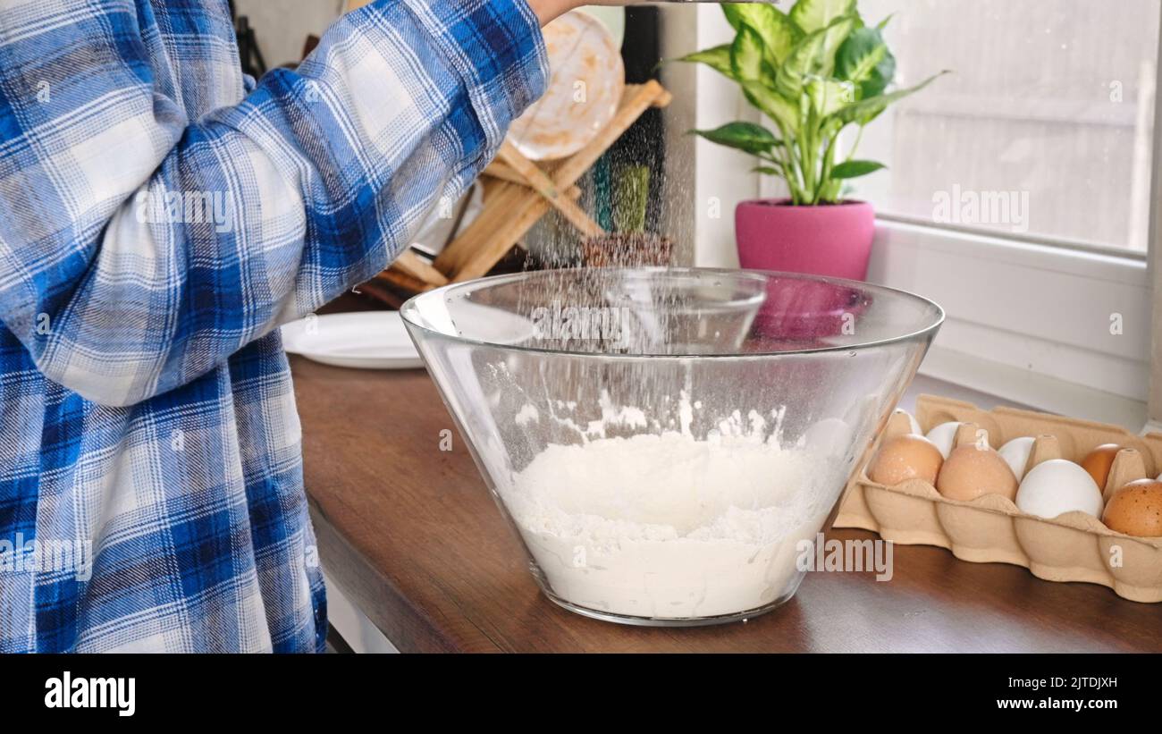 straining flour into a bowl with eggs in the background Stock Photo - Alamy