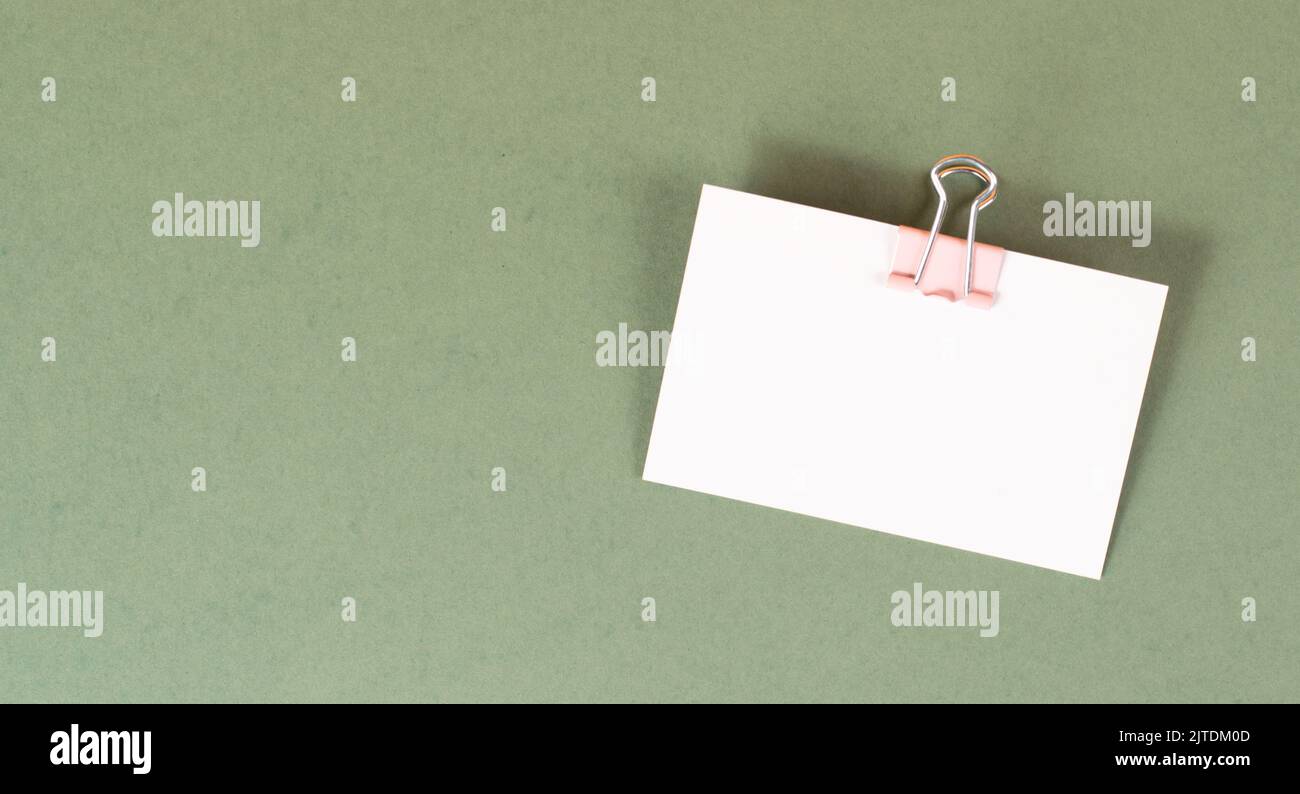 Blank white paper with a paperclip on a green colored background, copy ...