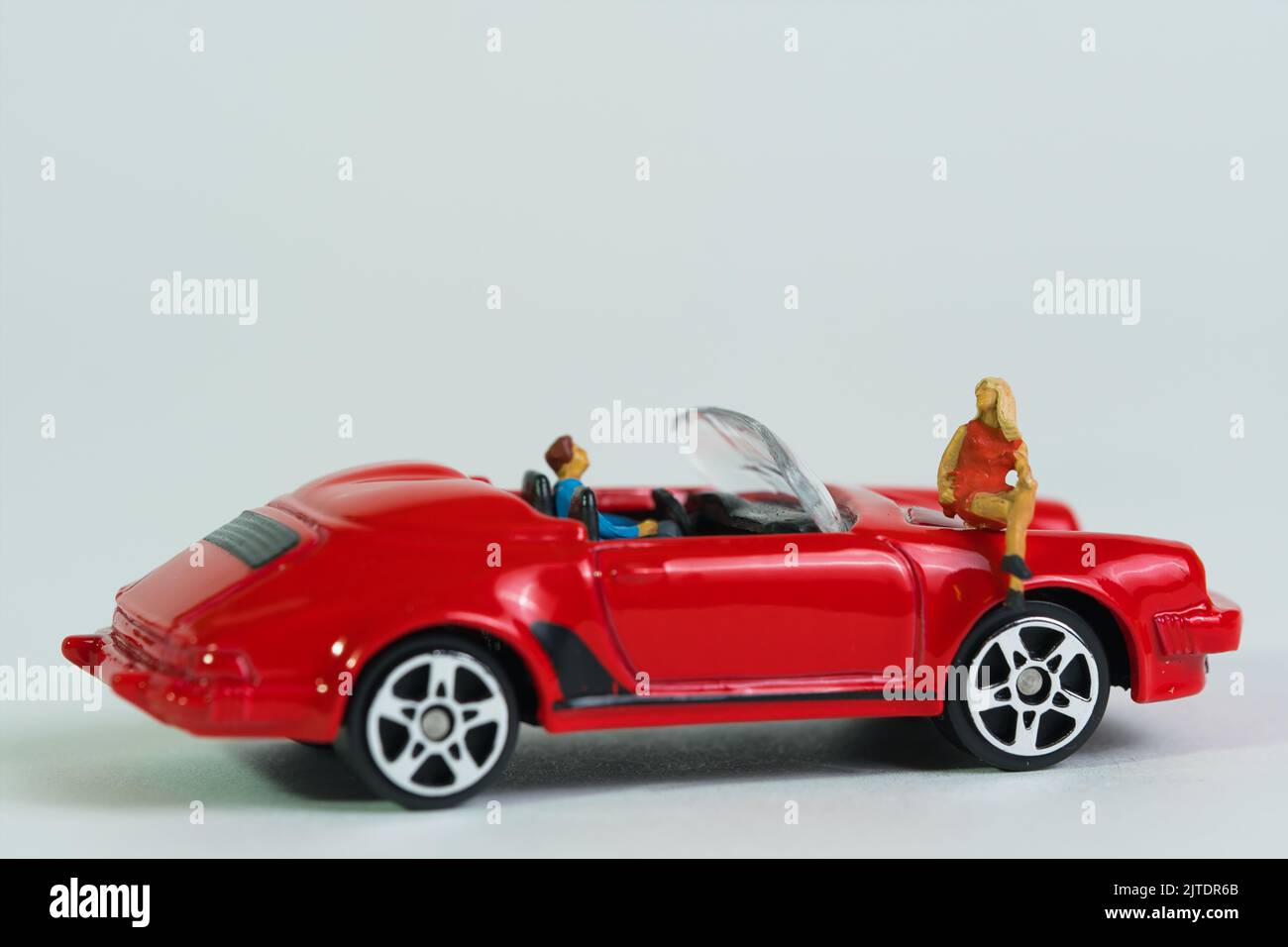 A woman sits on a red cabriolet sports car with driver, miniature ...