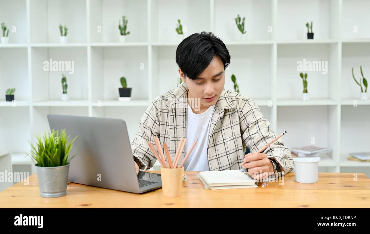 Smart young Asian male college student writing something on notebook ...