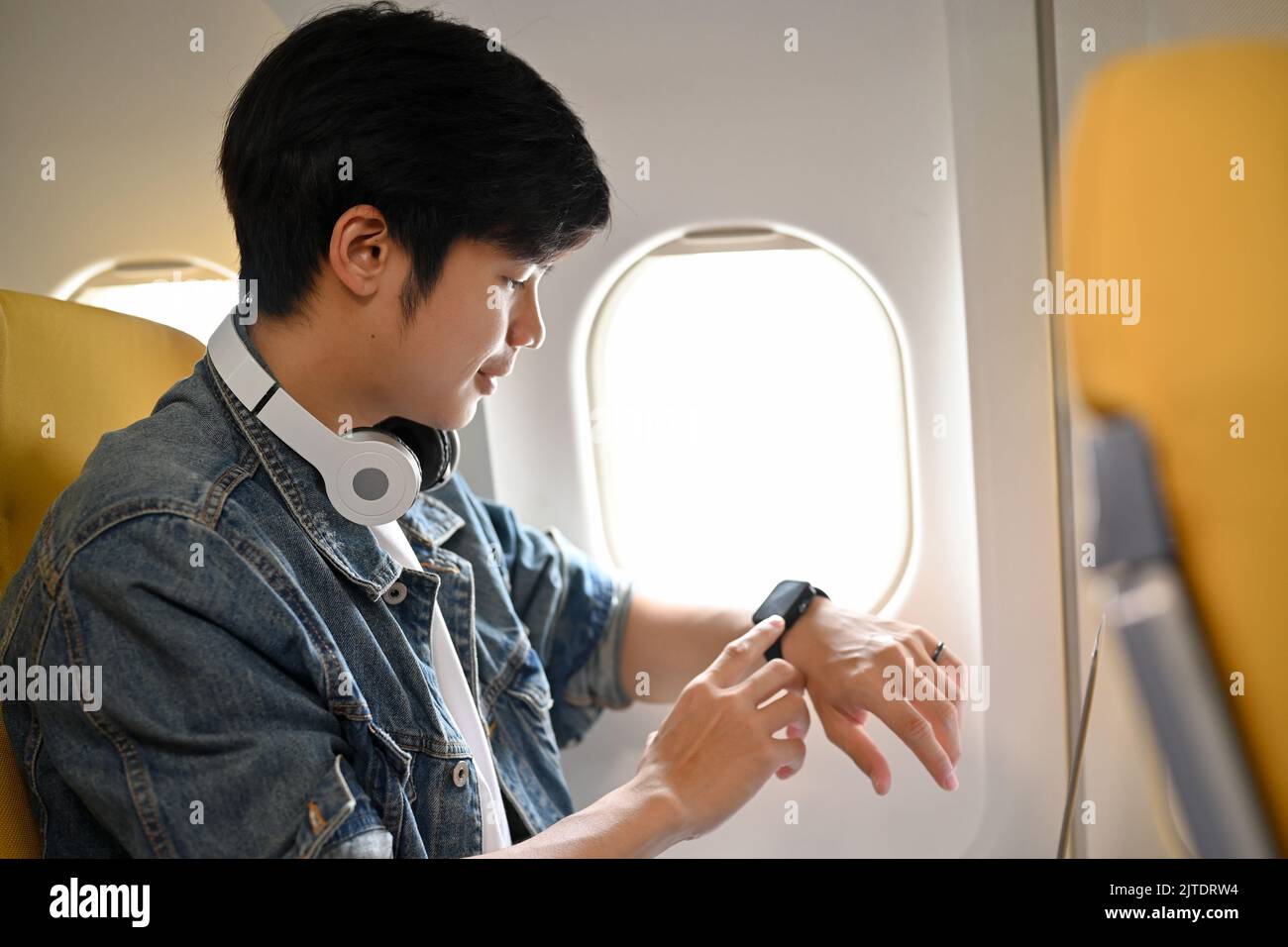 Handsome young Asian male passenger sits at a window seat in economy ...