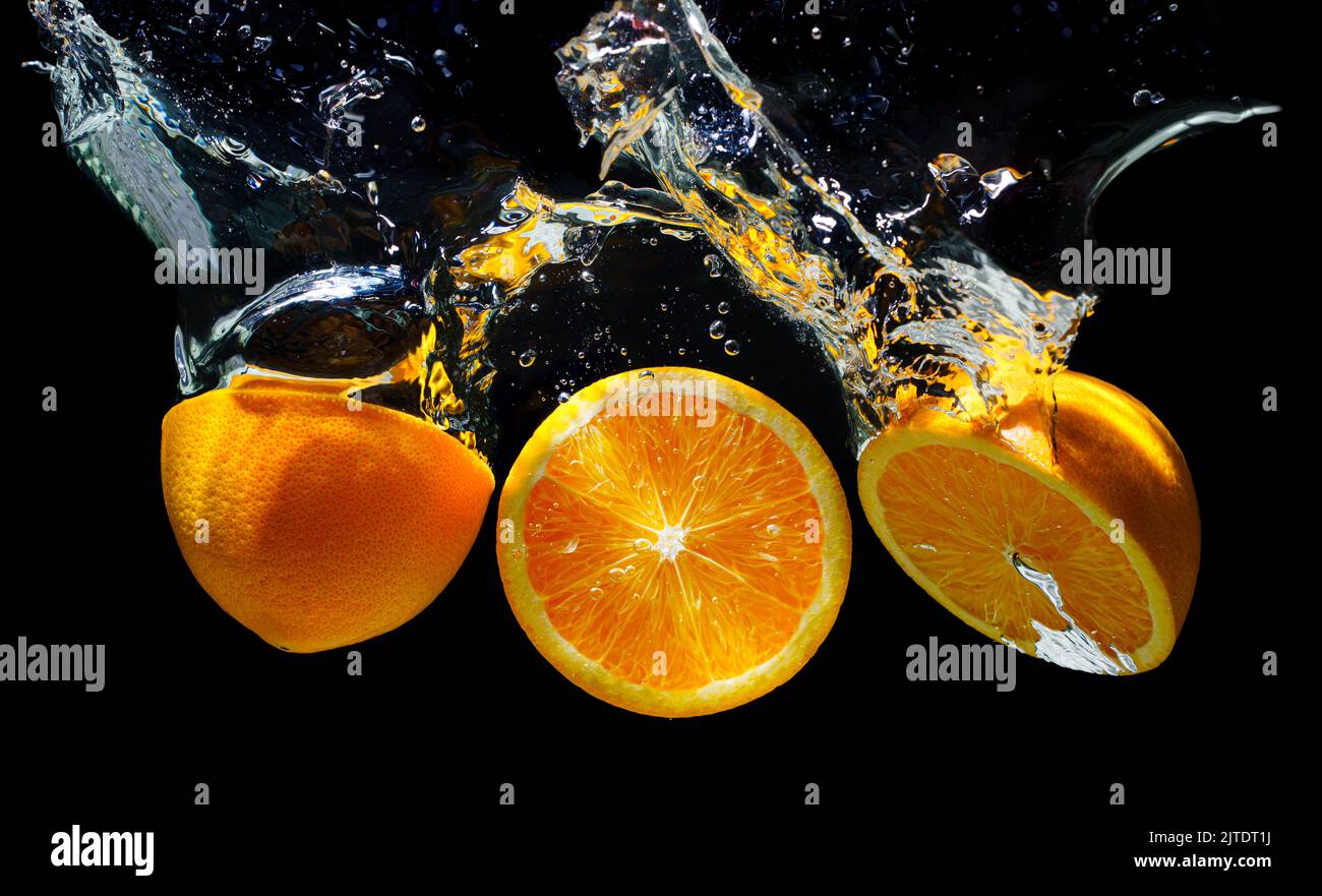 Three orange halves dropped in water with splashes isolated on black ...