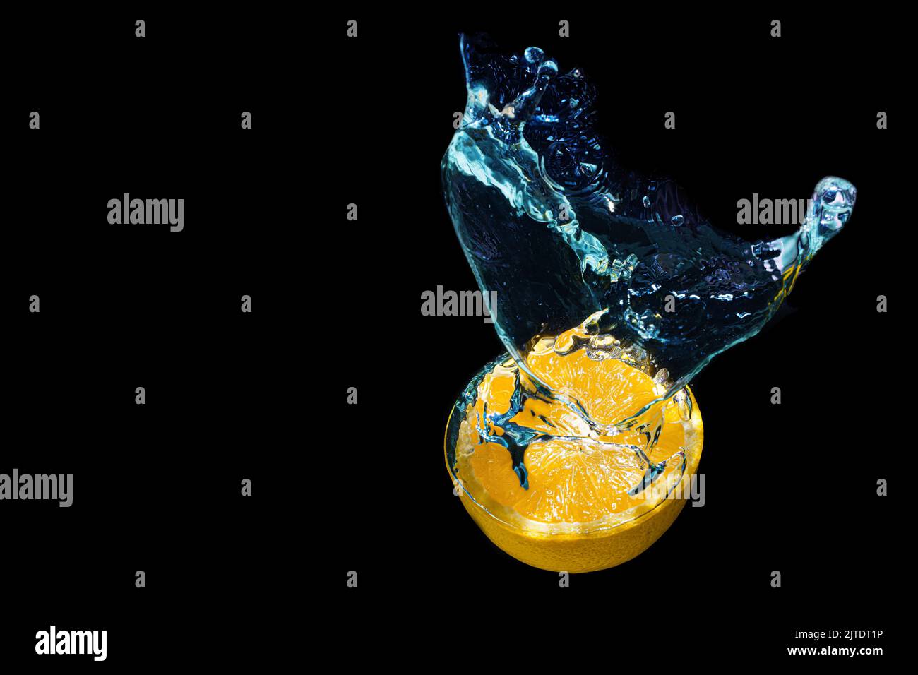 Fresh halved citrus fruit dropped in water with splashes on black ...