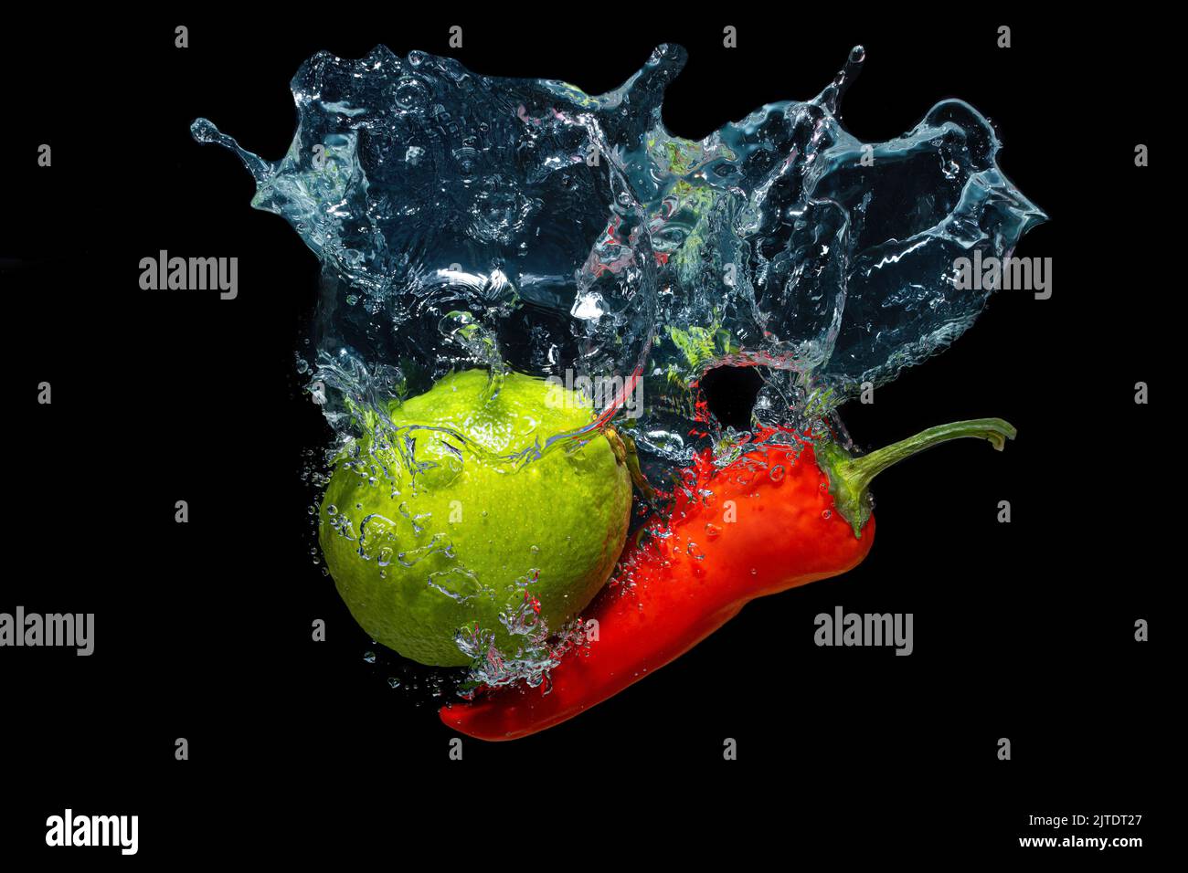 Hot red chilli and fresh whole lime dropped underwater with splashes ...