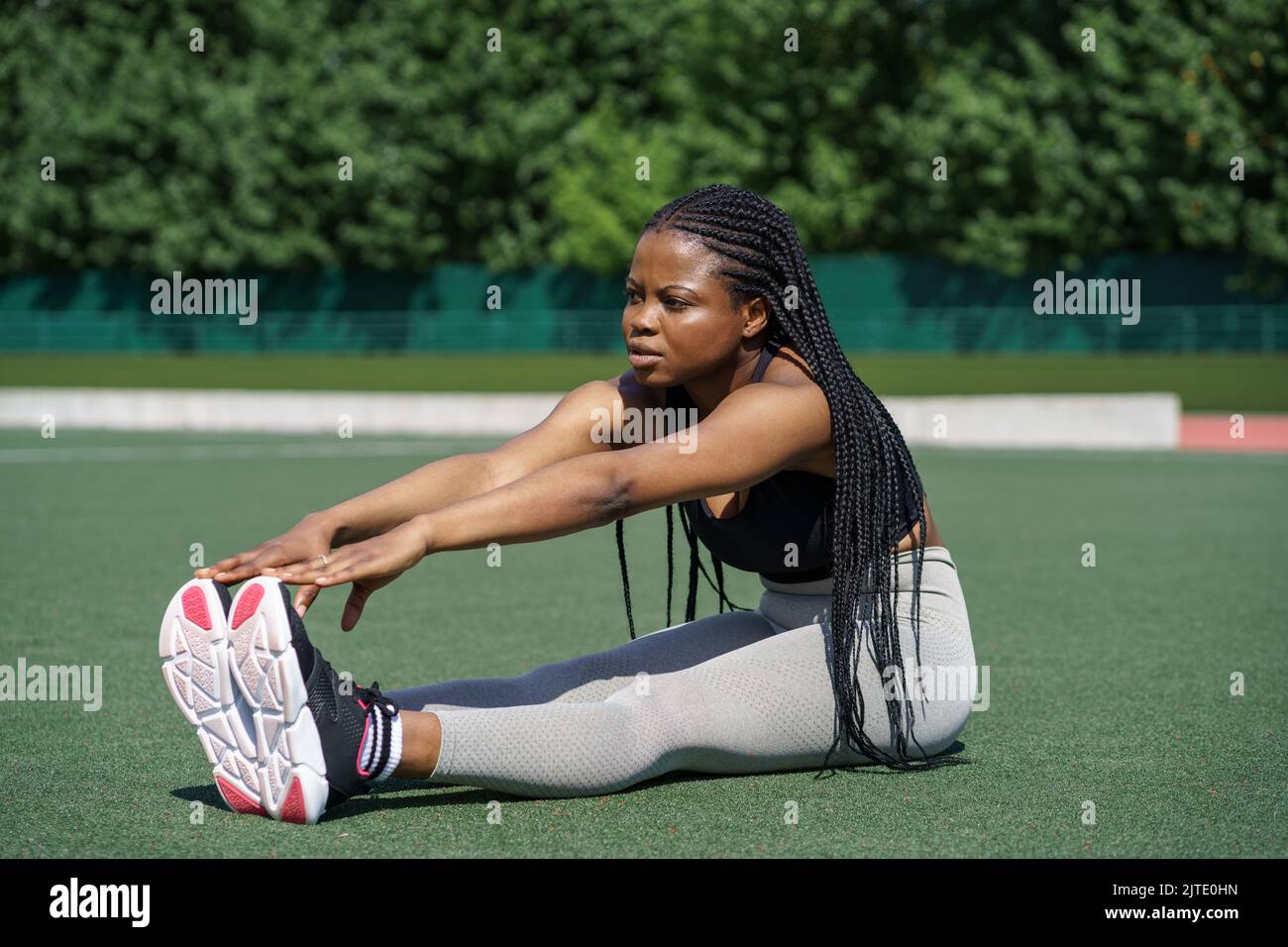 African American woman enjoys stretching back sitting on green turf ...
