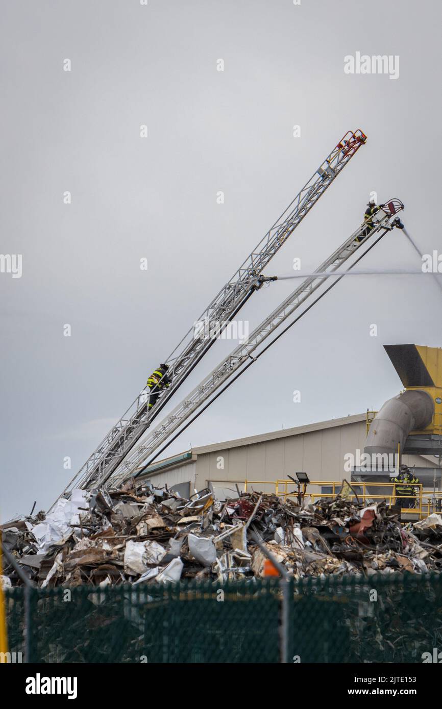 A firefighter using hose from a ladder at an industrial fire Stock ...