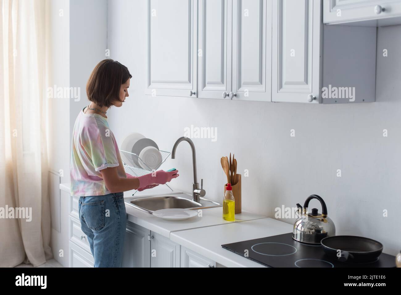 Side view of woman cleaning plate near dishwashing liquid in kitchen ...