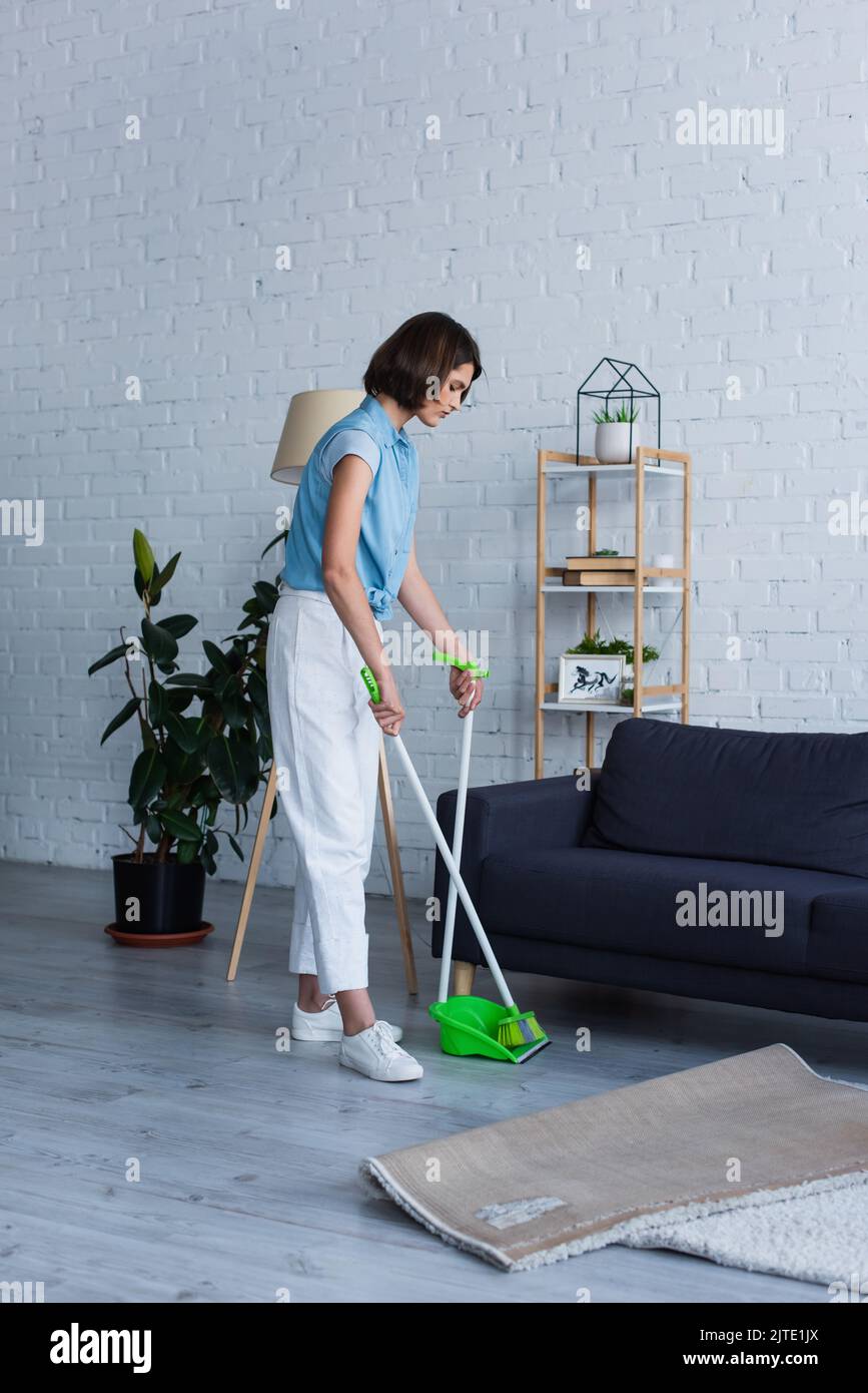 full length of young woman sweeping floor with broom in living room Stock Photo - Alamy