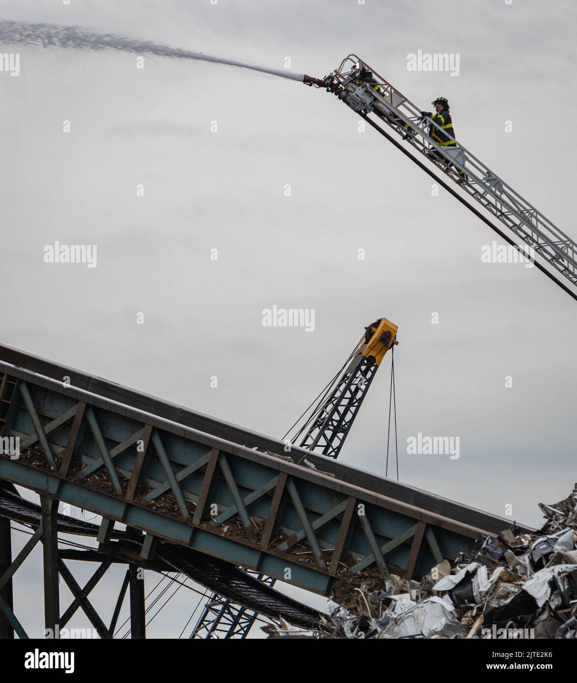 A firefighter using hose from a ladder at an industrial fire Stock ...