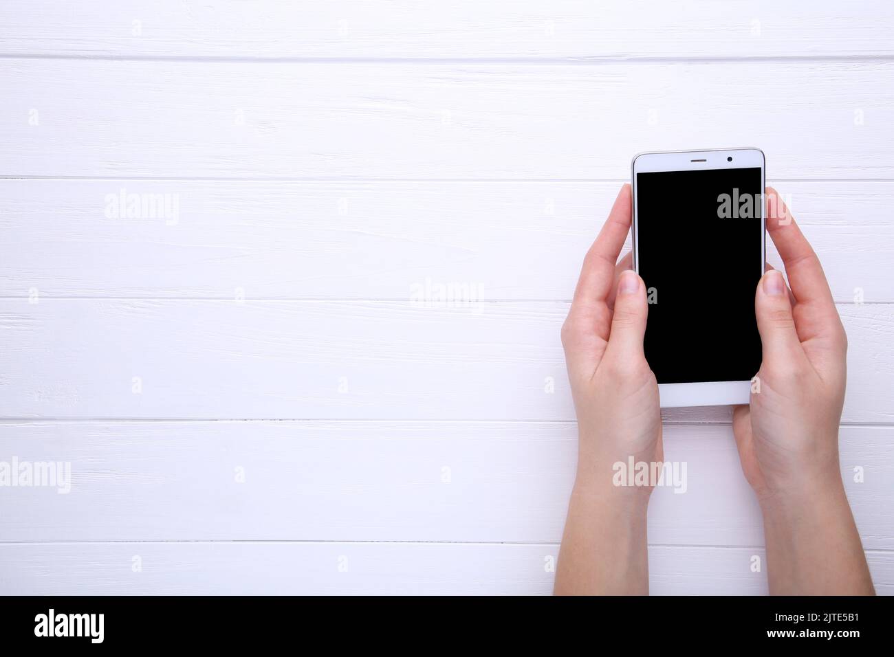 Female hands holding mobile phone with blank screen on white wooden ... Female hands holding mobile phone with blank screen on white wooden ...