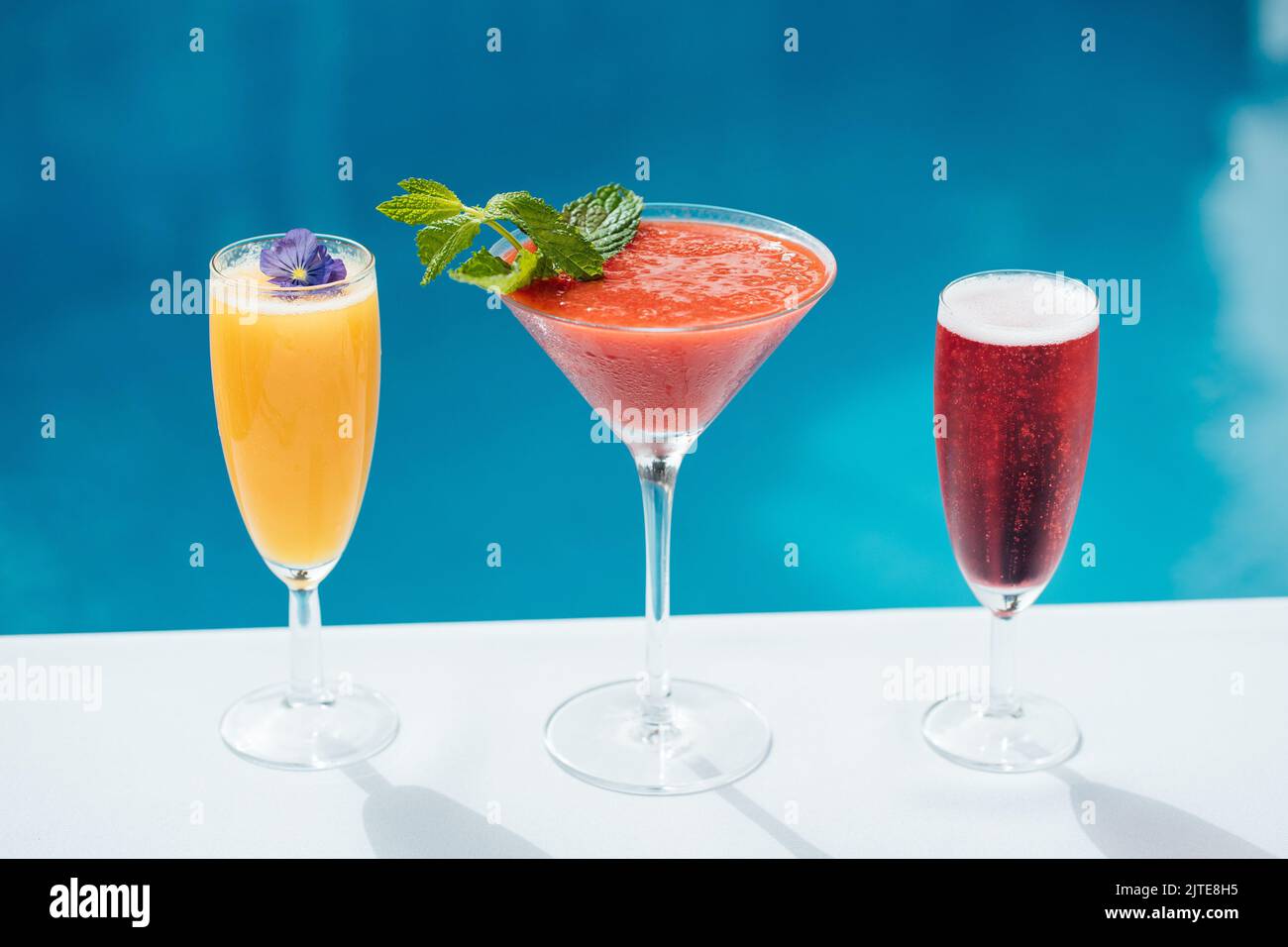 The view of three glasses cocktails on a white surface before the blue ...