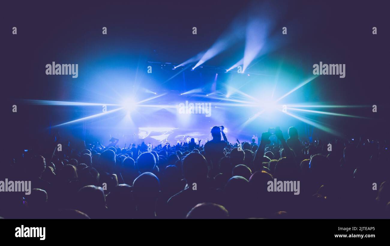 A crowded concert hall with scene stage lights in blue tones, rock show ...