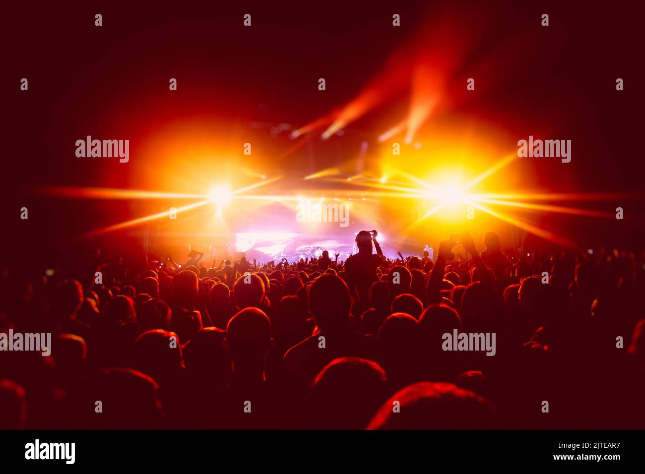A crowded concert hall with scene stage in red lights, rock show ...