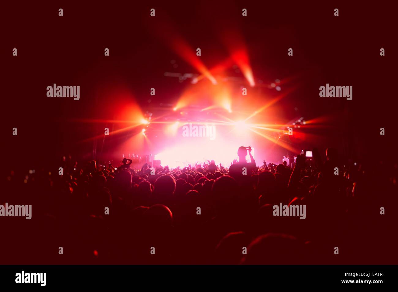 A crowded concert hall with scene stage in red lights, rock show ...