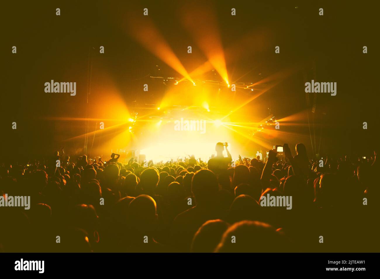 A crowded concert hall with scene stage orange and yellow lights, rock ...