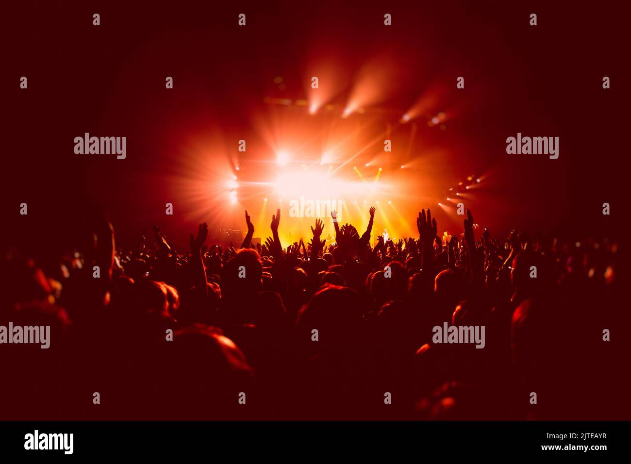 A crowded concert hall with scene stage in red lights, rock show ...