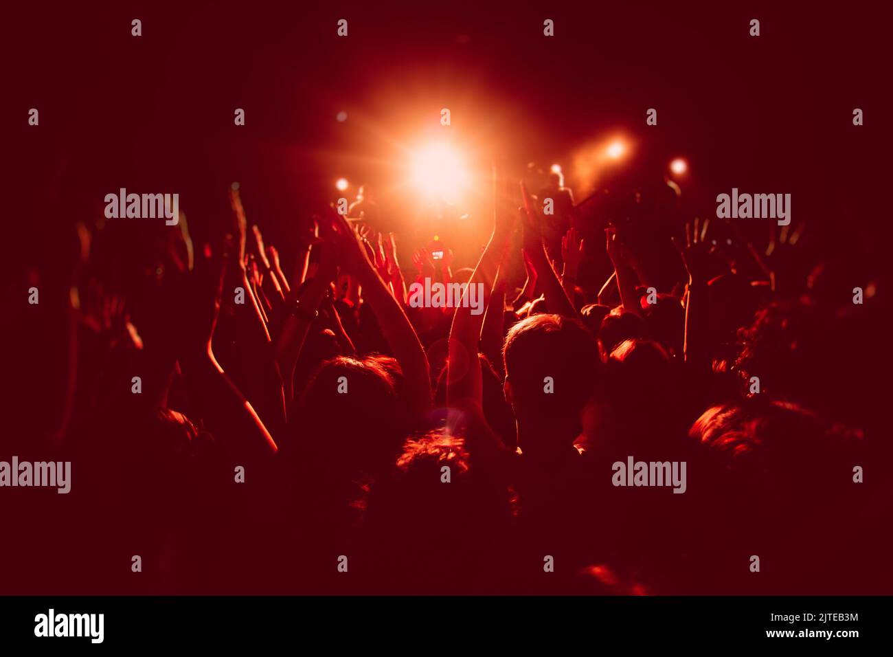 A crowded concert hall with scene stage in red lights, rock show ...