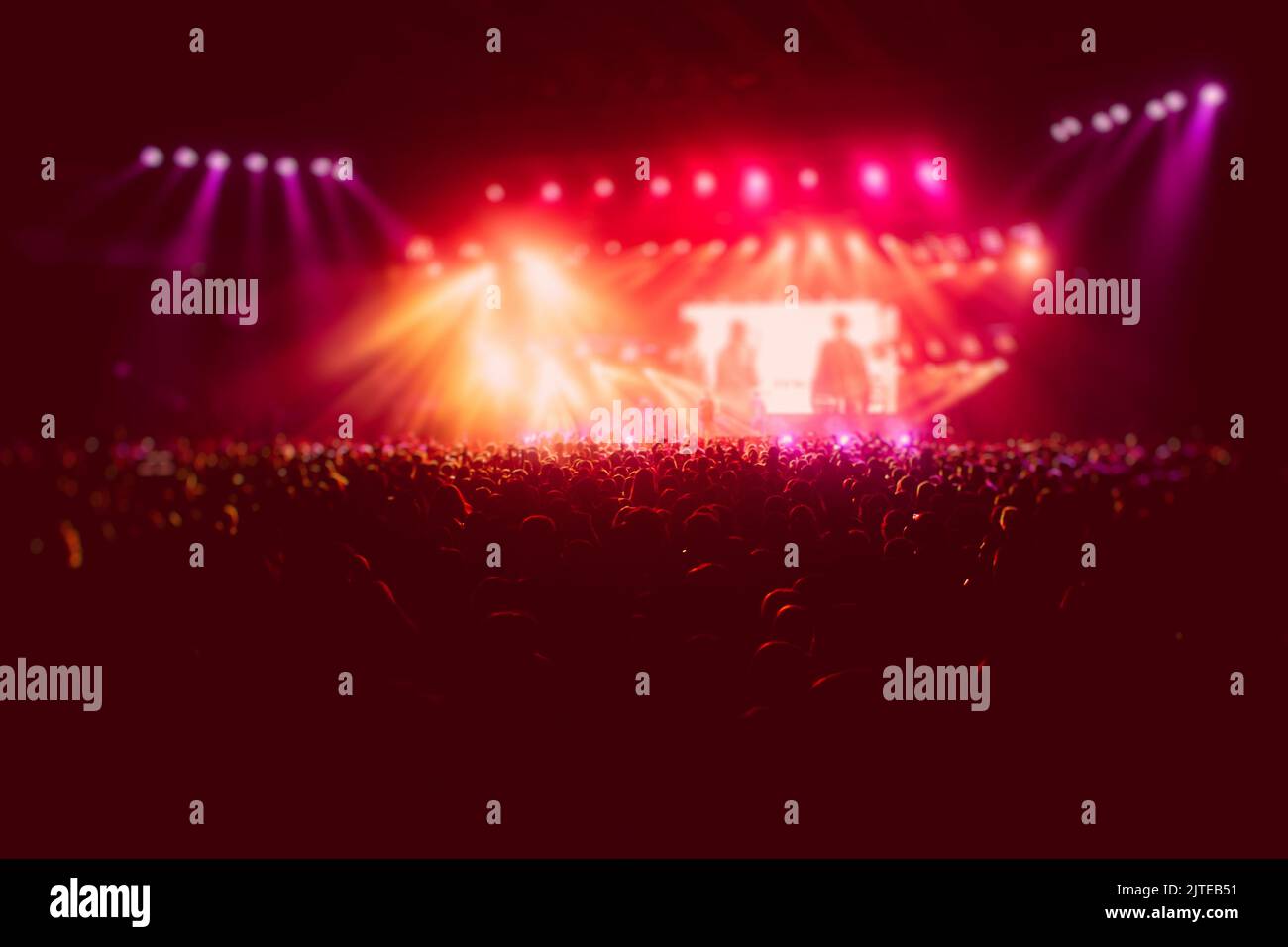 A crowded concert hall with scene stage in red lights, rock show ...