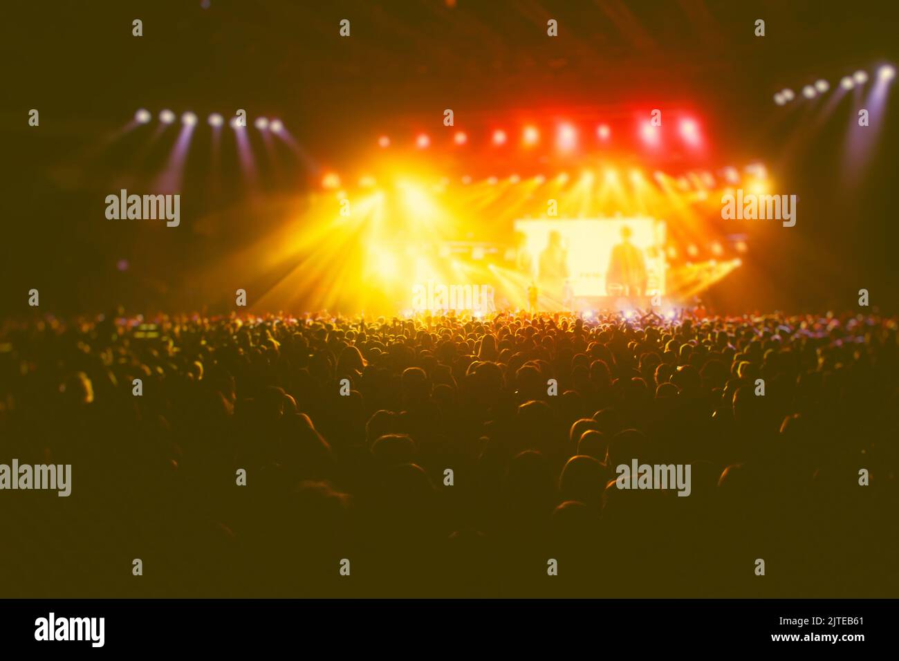 A crowded concert hall with scene stage orange and yellow lights, rock ...